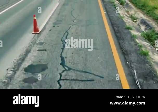 Road damage with cracks and warning cone on highway during daytime ...