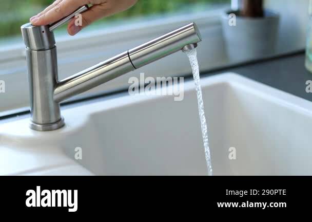 Close up of a female hand opening a tap in the kitchen, white sink and ...