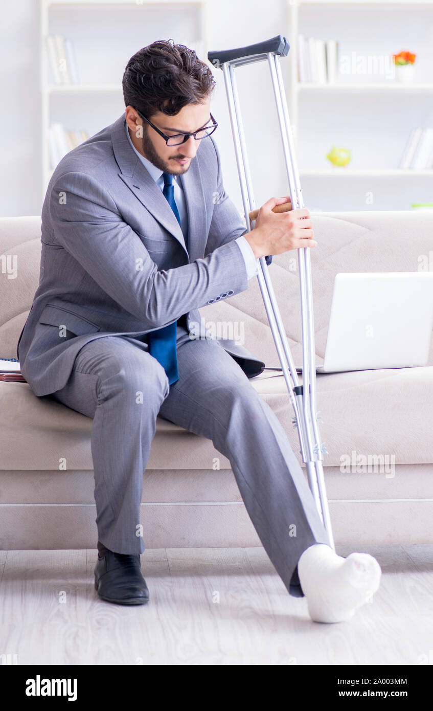 The businessman with crutches and broken leg at home working Stock ...