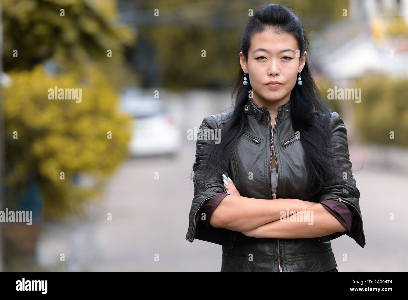 Portrait of beautiful Asian rebellious woman with arms crossed outdoors ...