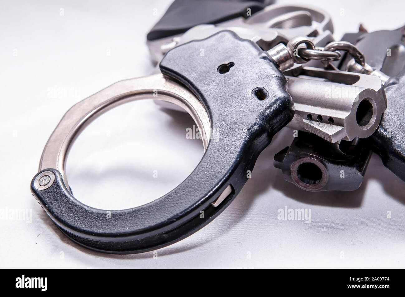 A set of two toned metal handcuffs on top of two revolvers, one black ...