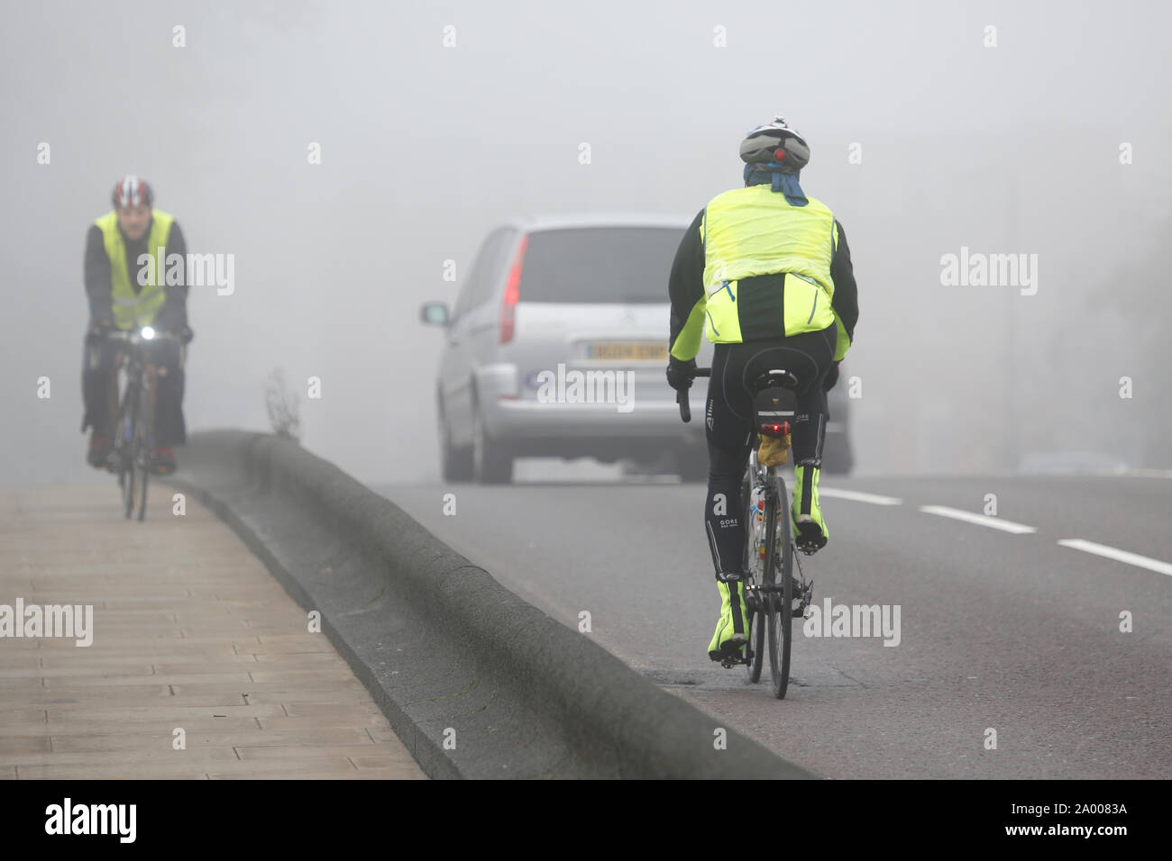 Cyclists riding, bicycle commuters, in heavy fog, a cold bad weather ...