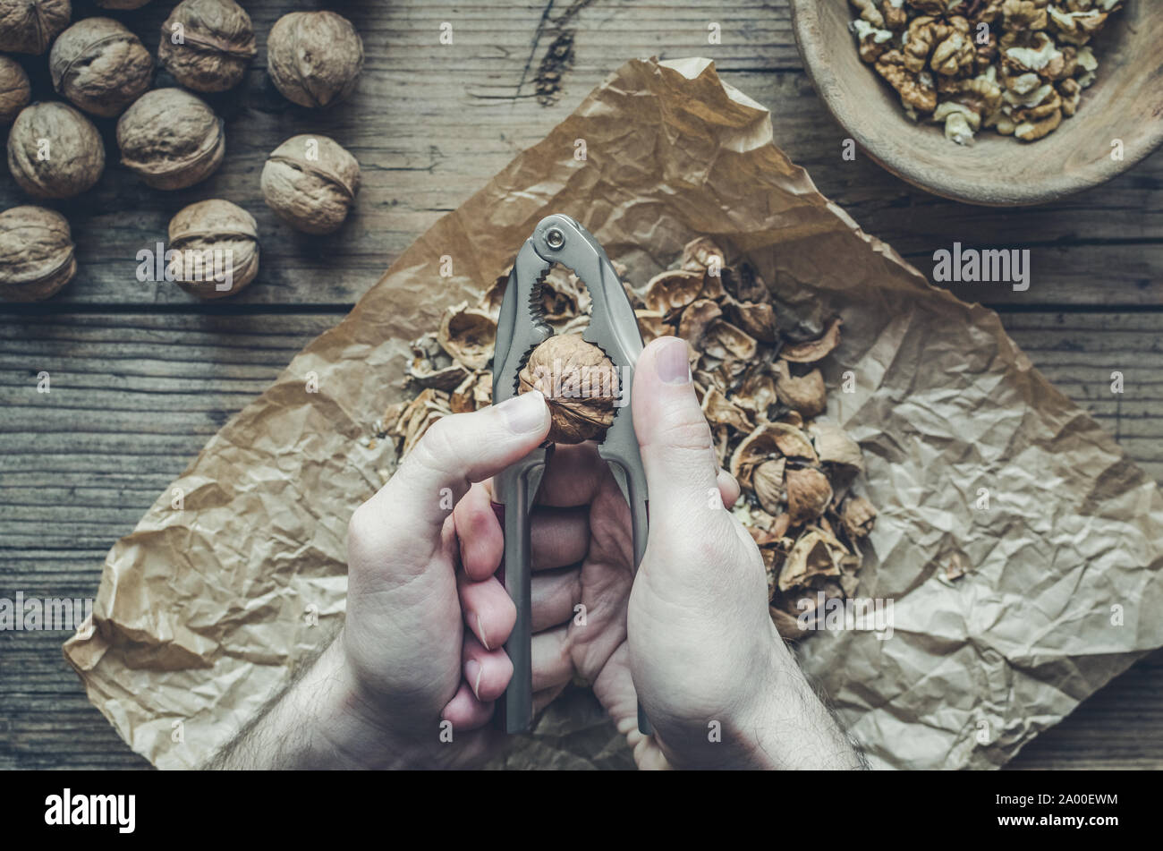 Man squeezes walnuts with nut cracker on wooden table Stock Photo - Alamy