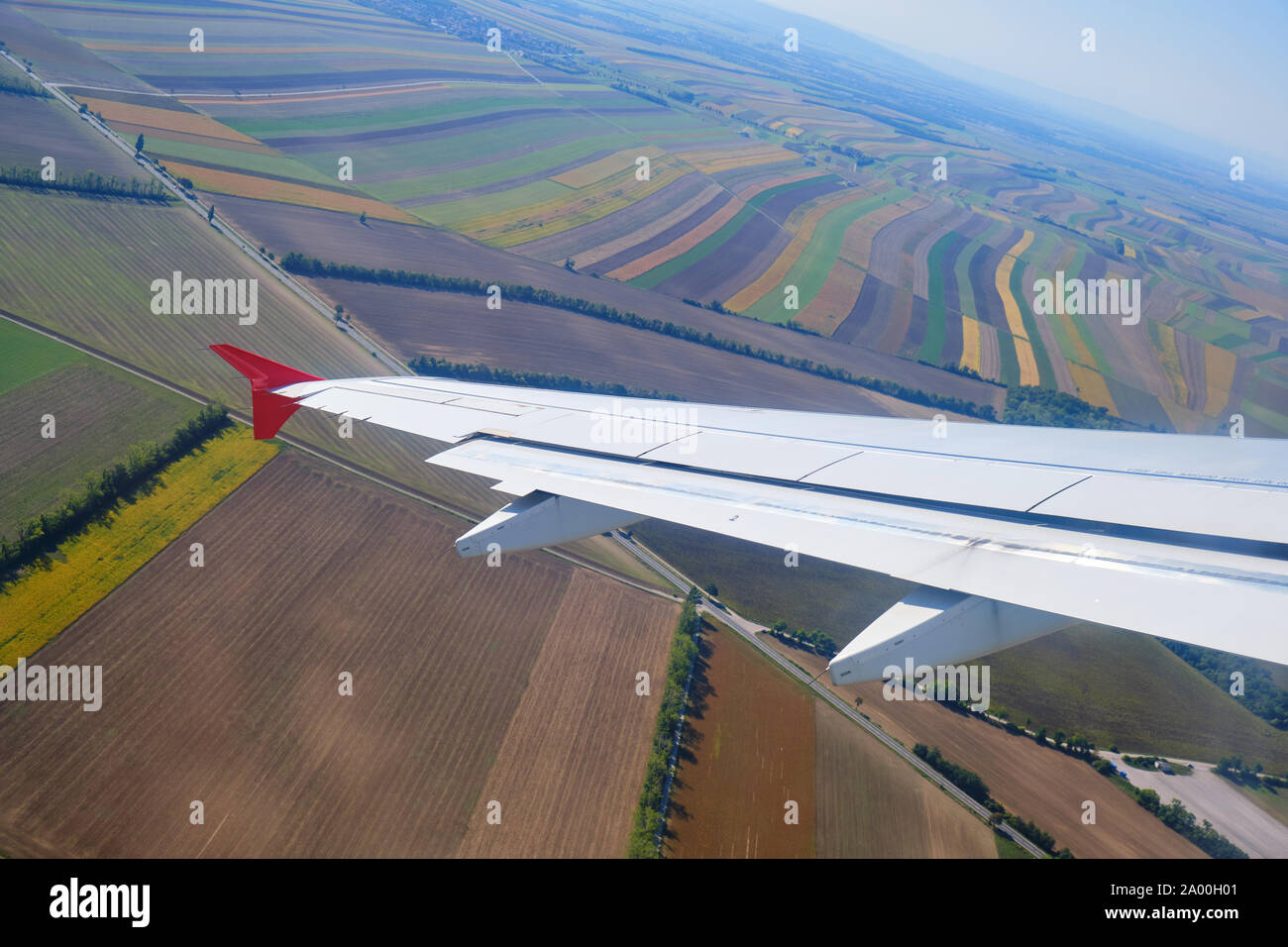 White airplane wing tilted in low flight over a crop fields pattern ...