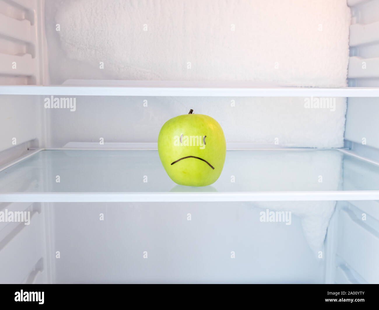 One green sad apple in open empty refrigerator with frozen ice on the ...