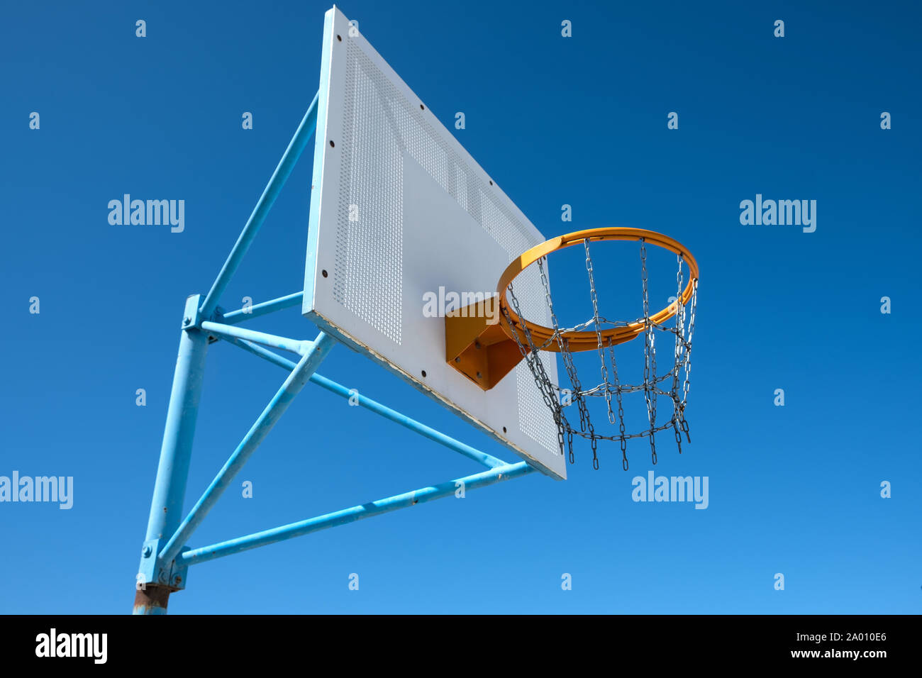 side view of a street basketball hoop with metal mesh over blue sky ...