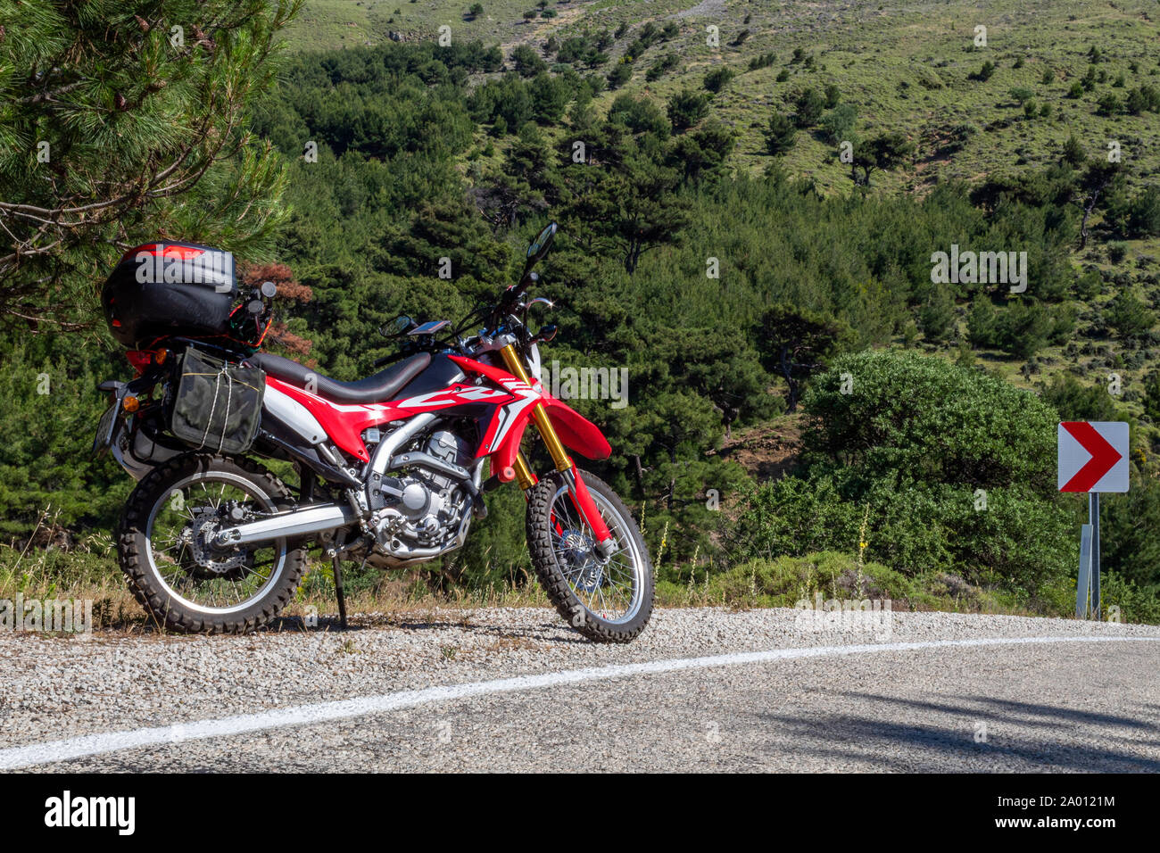 A red enduro motorcycle on the left side of the road, the forest is in ...