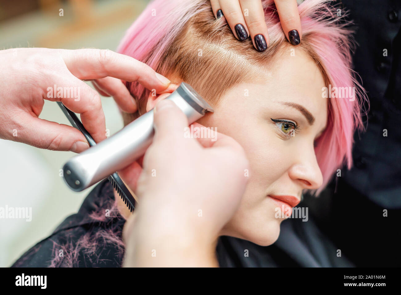 a barber shaves temple woman pink hair with electric shaver in beauty ...