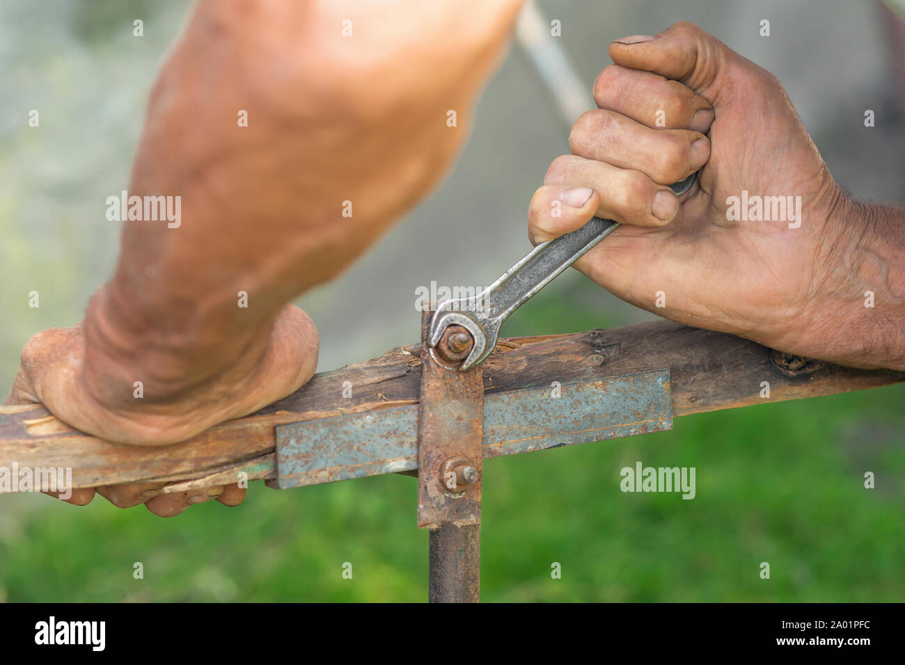 a hand of an elderly man is twisting the nut with a wrench outdoors ...