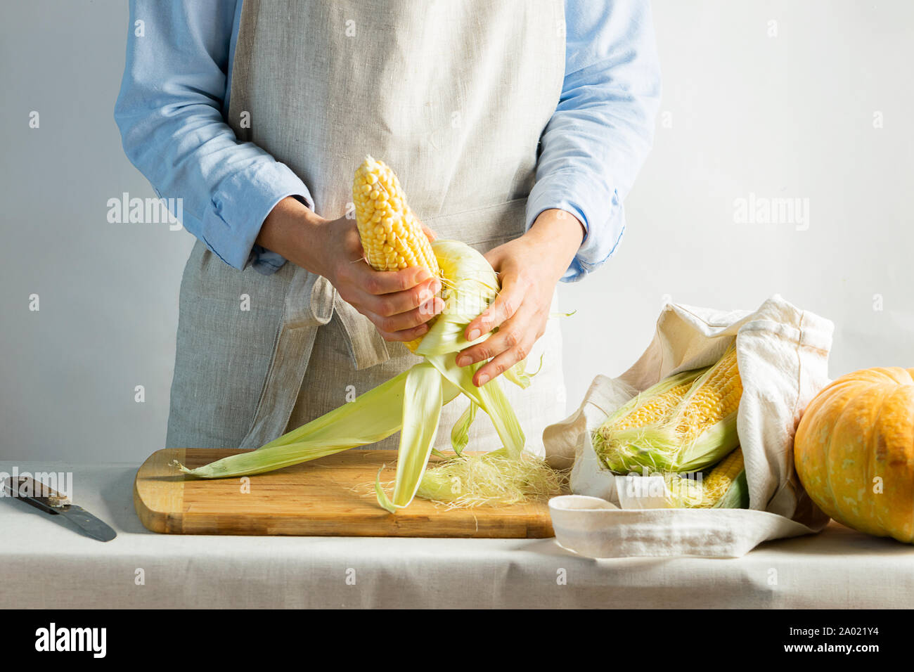 A female cook a cotton apron cleans ripe corn on the cob. Rustic ...