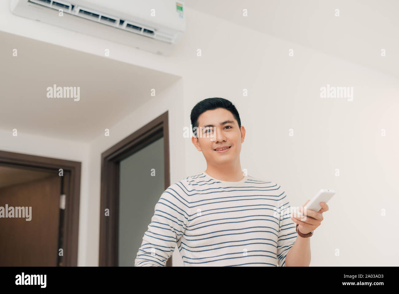 Portrait of happy man using remote control to operate air conditioner ...