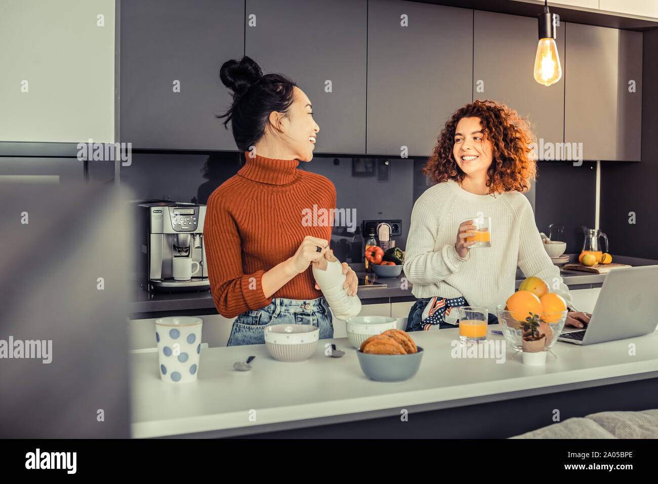 Two smiling roommates standing together at the kitchen table preparing ...
