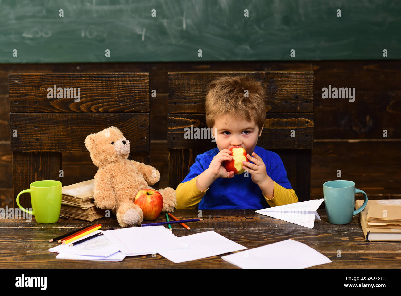 School break. Hungry kid biting apple in classroom. Small boy playing ...
