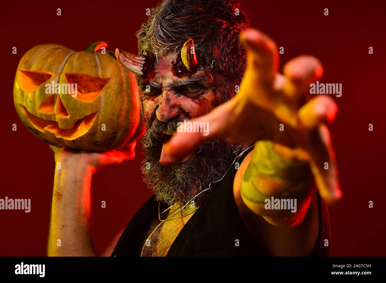 Halloween darkness and light concept. Man devil hold pumpkin on red ...
