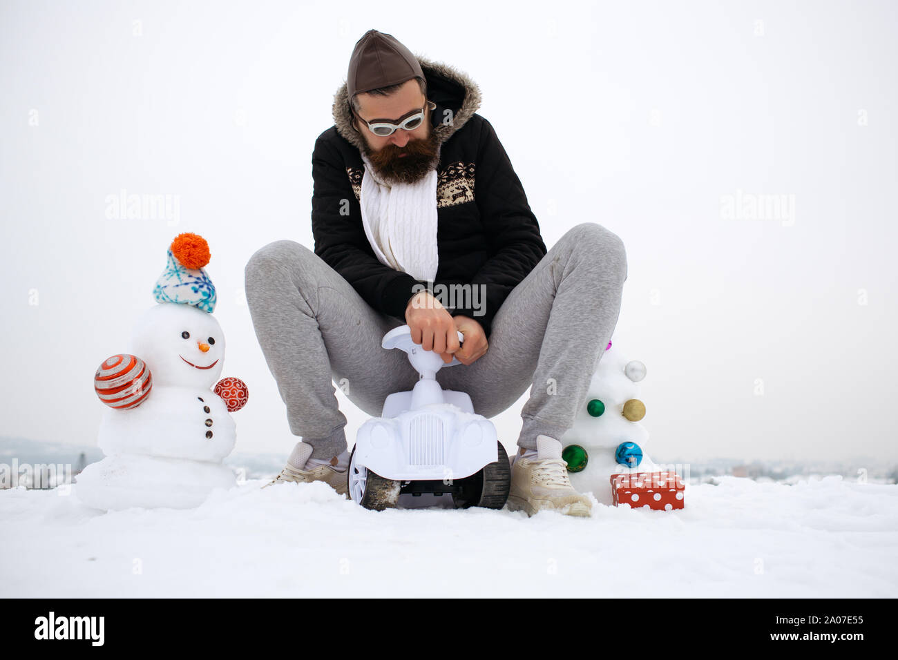 Hipster riding toy car on white sky. Bearded man in pilot glasses and ...