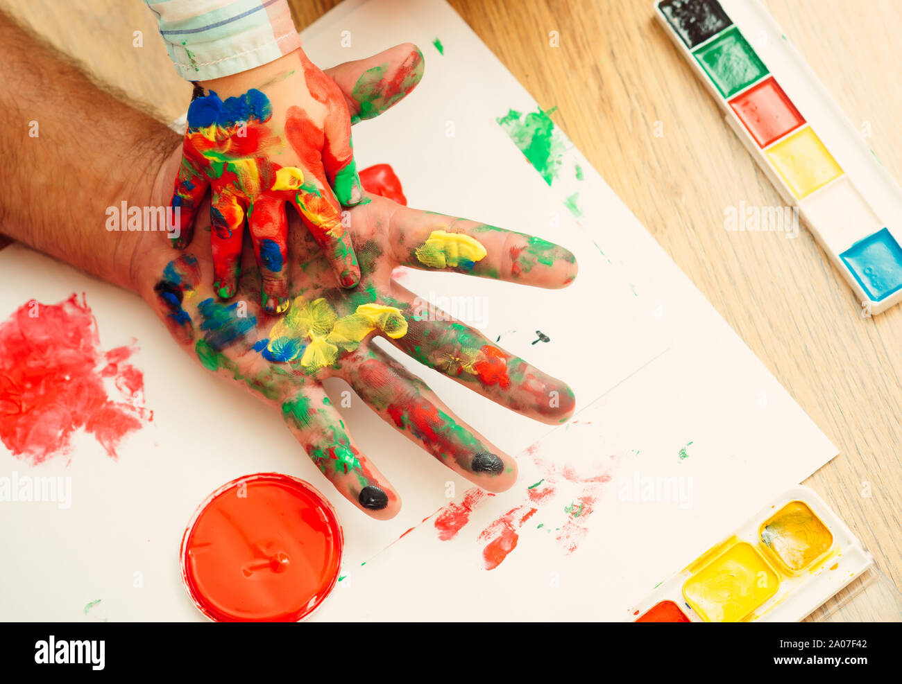 Hands in colorful paints and multicolor palette on white paper. Arts ...