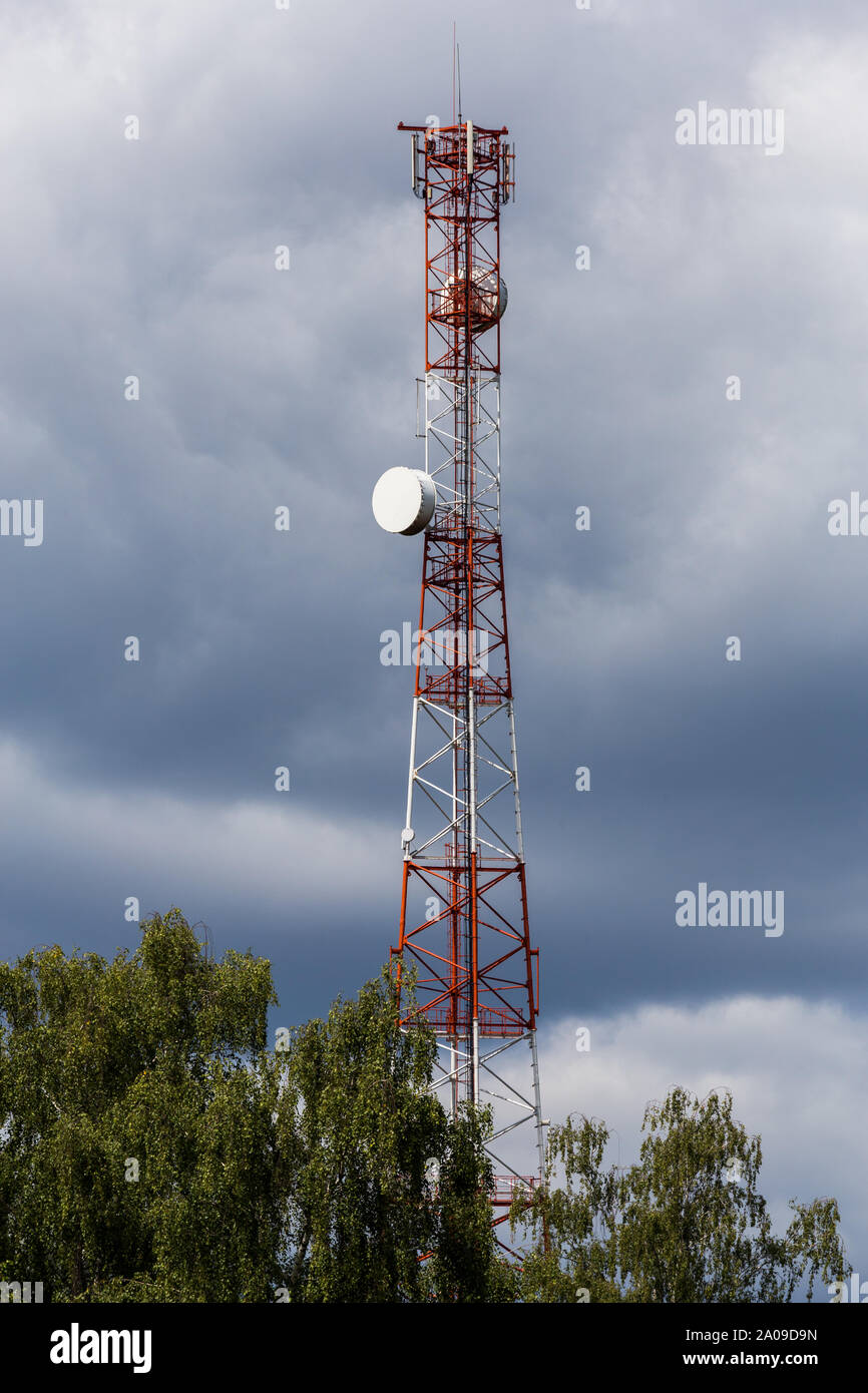 Red-white telecommunication tower with top of green tree on blue sky with clouds background ...