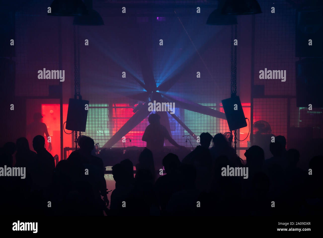 Techno night club with a clubbing crowd and a DJ behind a turntable ...