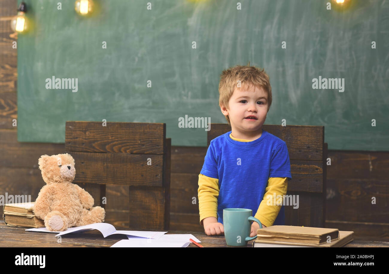 Little kid standing behind wooden desk. Dark wood table with copybooks ...