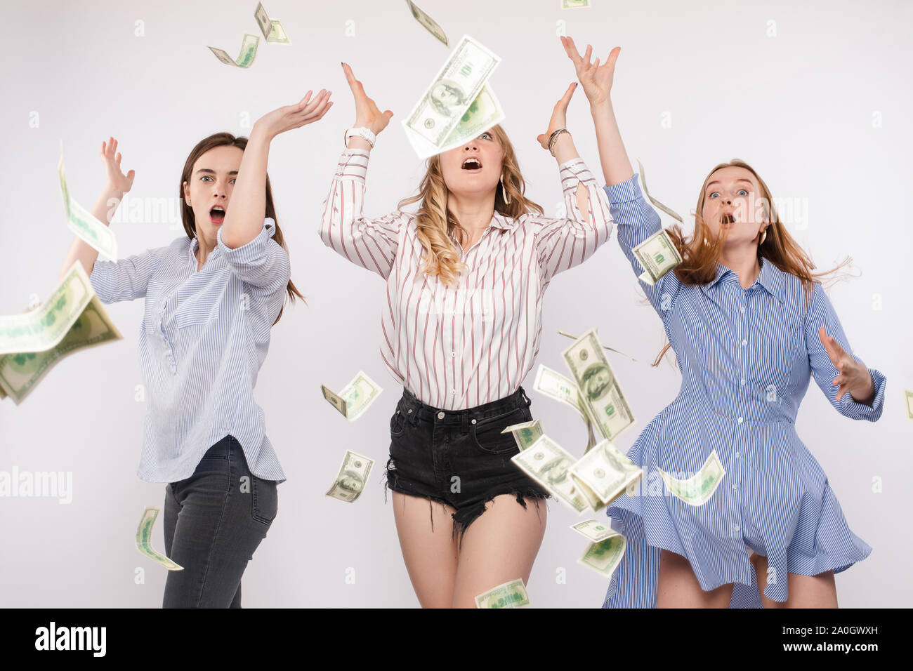 Three excited and shocked women with arms up trying to catch flying ...