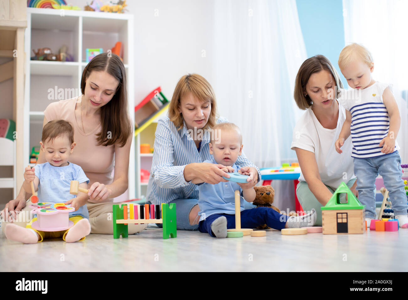 Babies with adults play in creche or kindergarten Stock Photo - Alamy