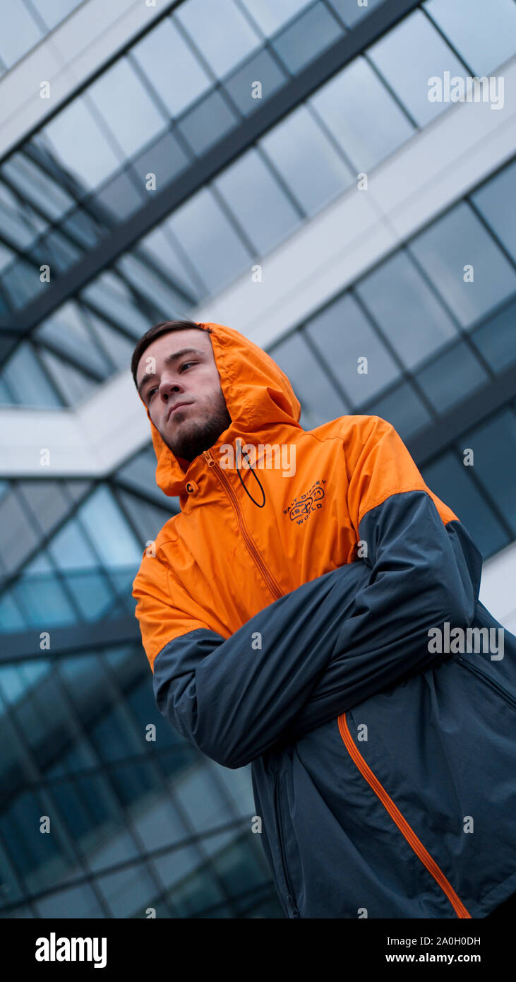Young man in orange work uniform - blue glass building on background ...