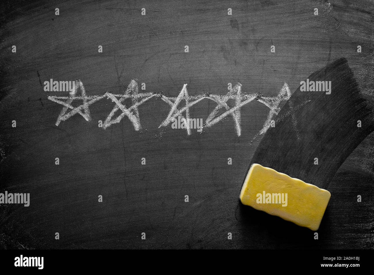 Erasing one star out of five hand drawn in white chalk on a chalkboard ...