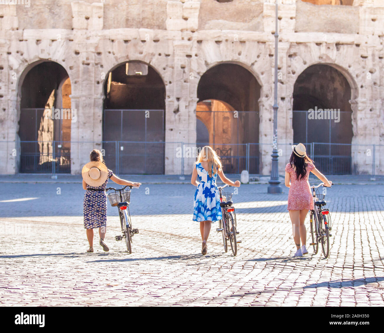 Three happy young women friends tourists with bikes at Colosseum in ...
