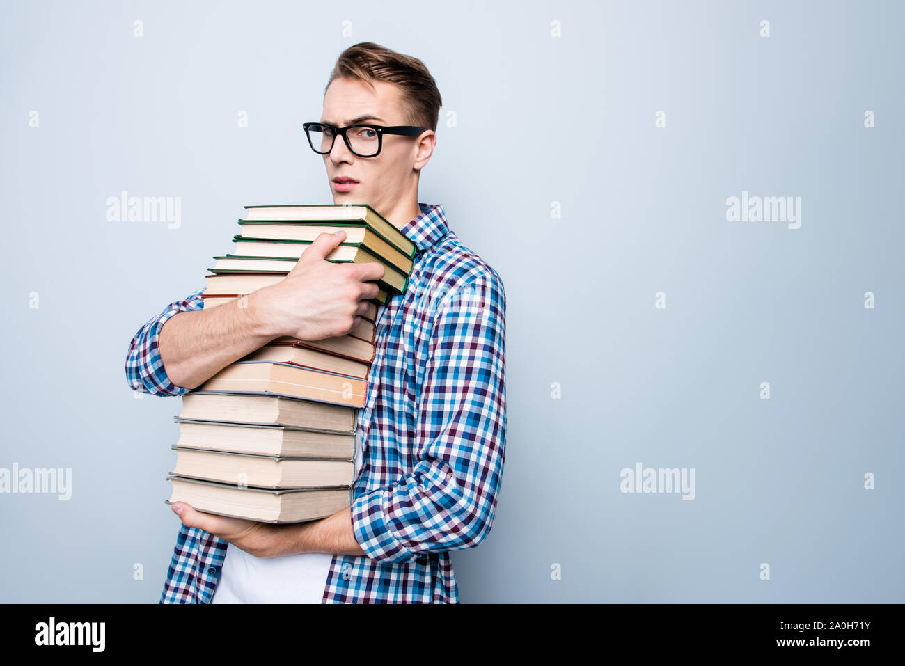 Portrait of upset, grumpy teen, teenager reader man hug pile of books ...