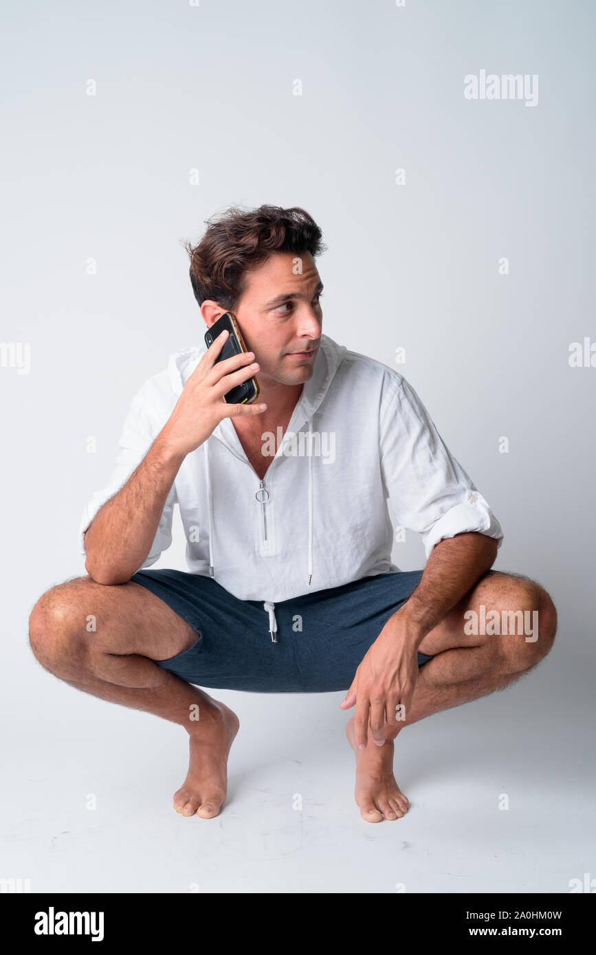 Full body shot of handsome Hispanic man crouching while talking on the ...