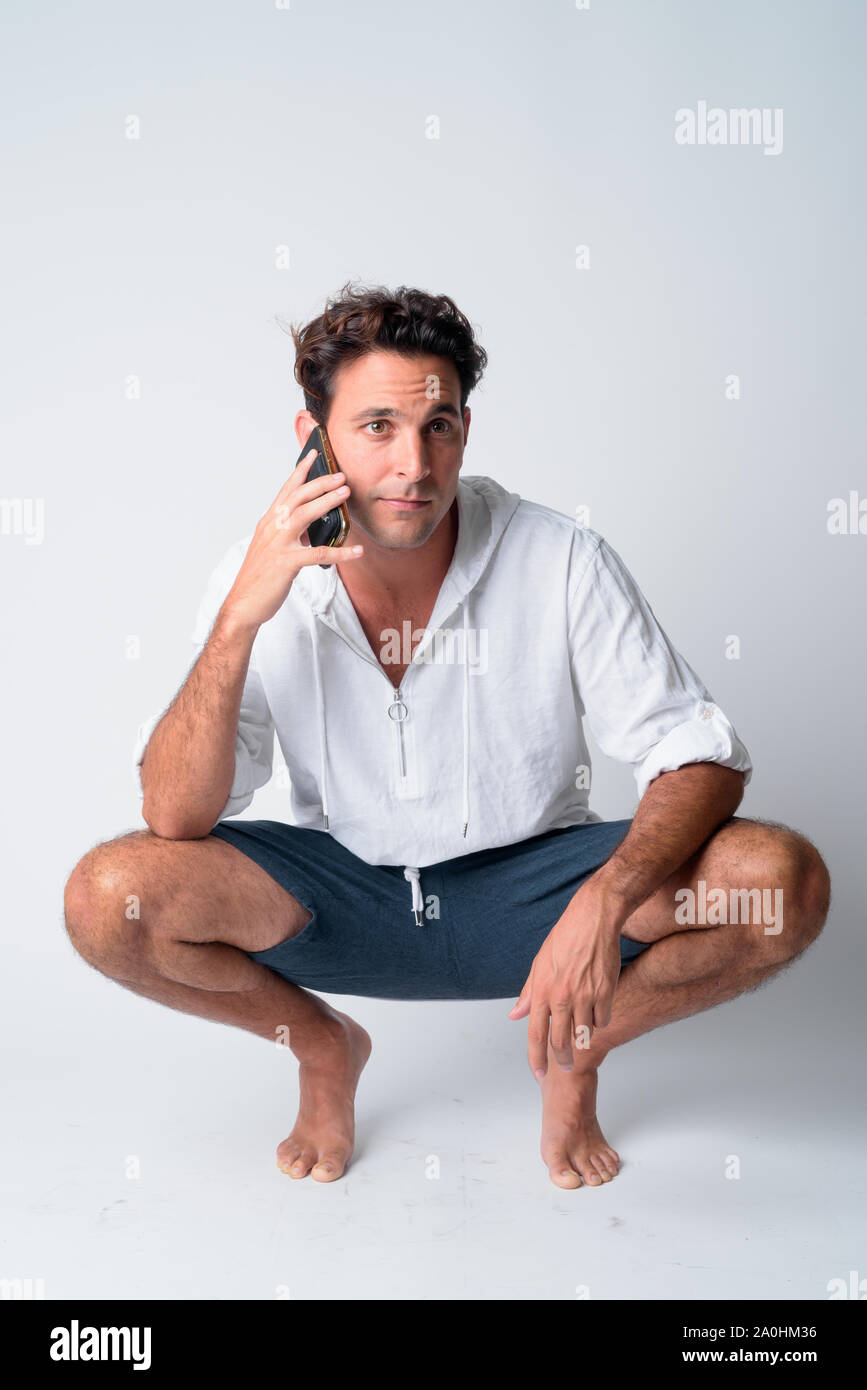 Full body shot of handsome Hispanic man crouching while talking on the ...