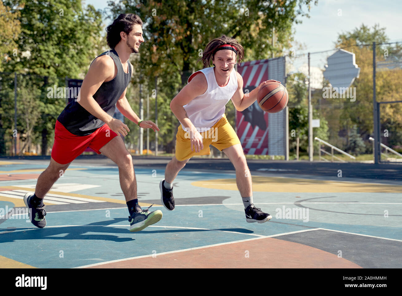 Photo of two sporty men playing basketball on playground on summer day ...