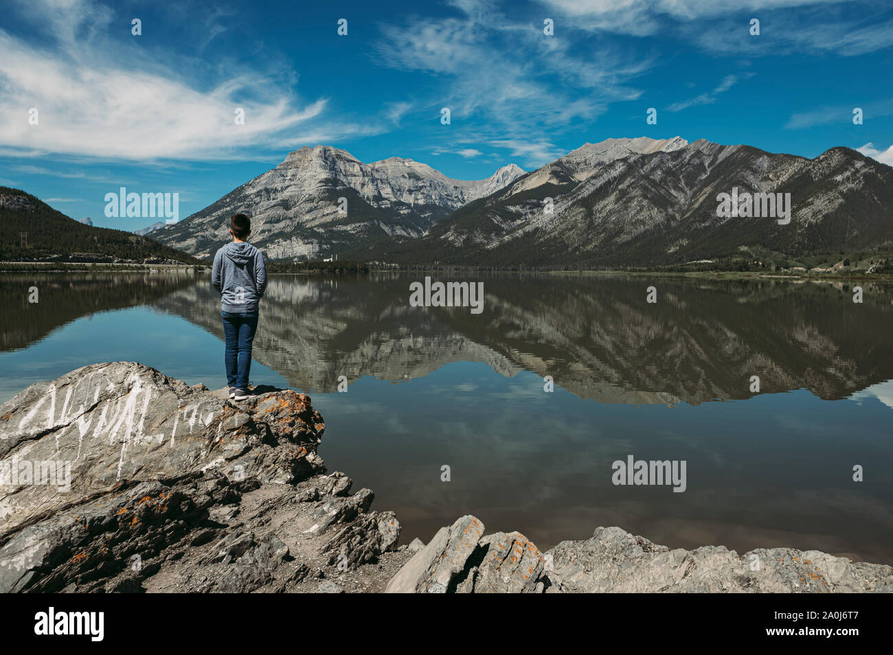 Boy standing on rocky ledge overlooking a lake and mountain vista Stock ...
