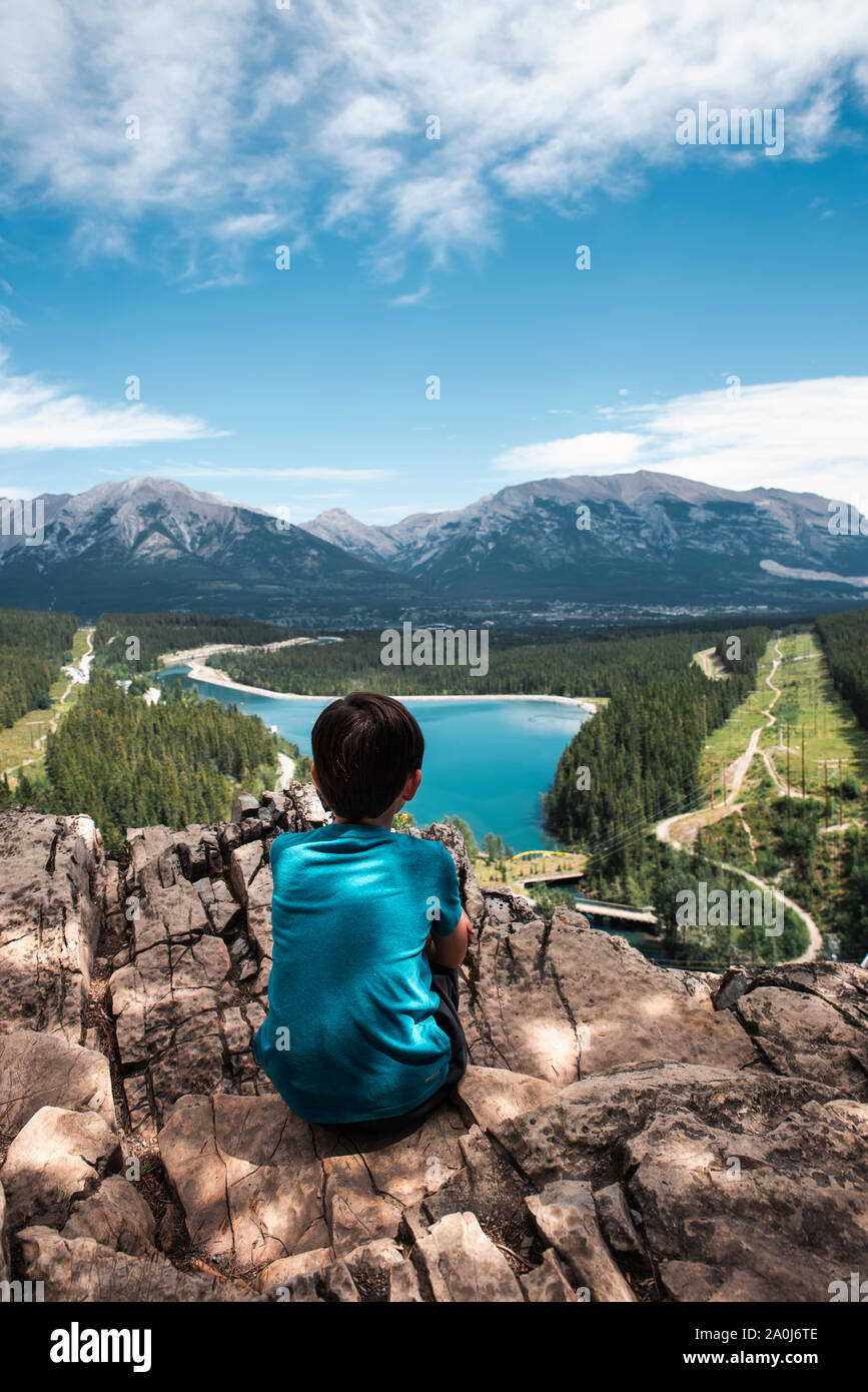 Young boy sitting on rocky ledge overlooking a lake and mountains Stock ...