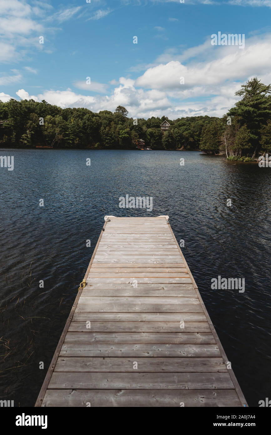 An empty dock on a lake with trees and cottages in background Stock ...