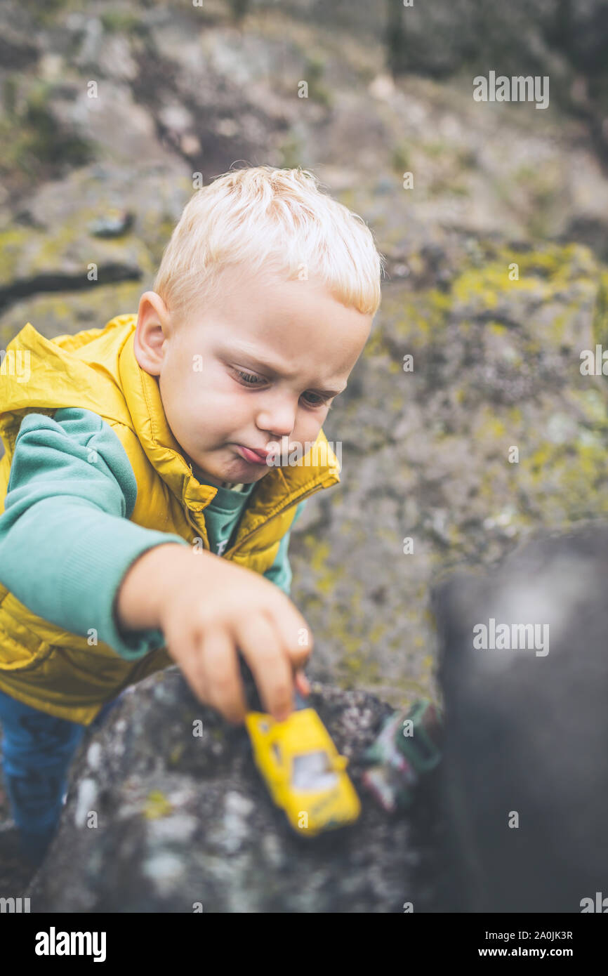 Toddler boy playing with toys on a rock. Little child walking on rocky ...