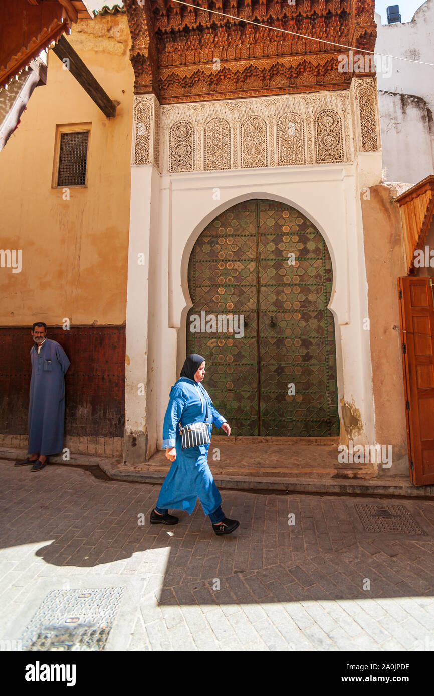 woman in traditional clothing walking past ornate mosque door in the ...