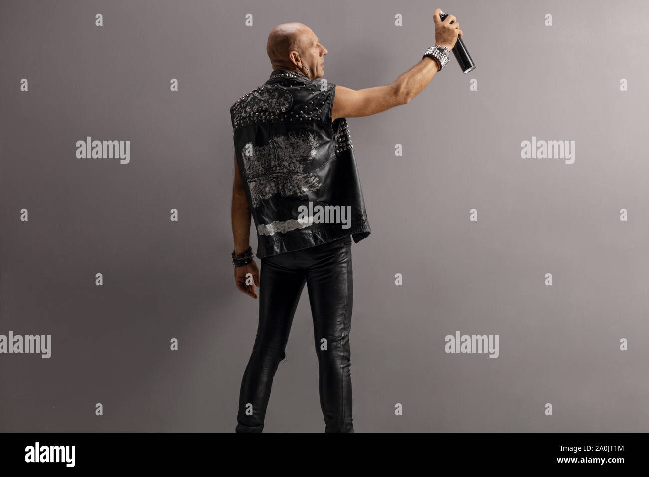 Mature punk in leather vest holding a spray for graffiti against a gray ...