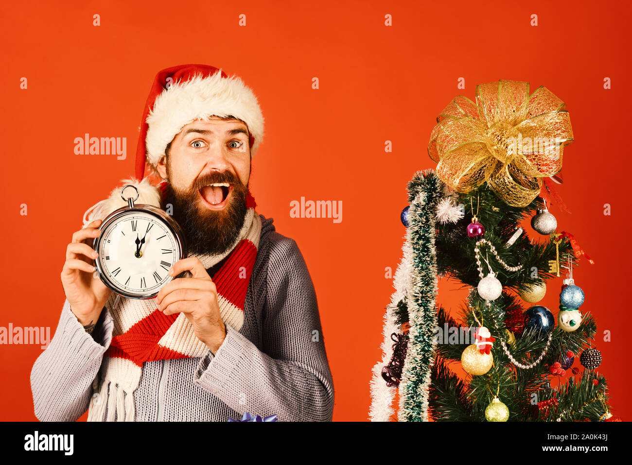 Guy or hipster in red hat holds big alarm clock. Man with beard and ...
