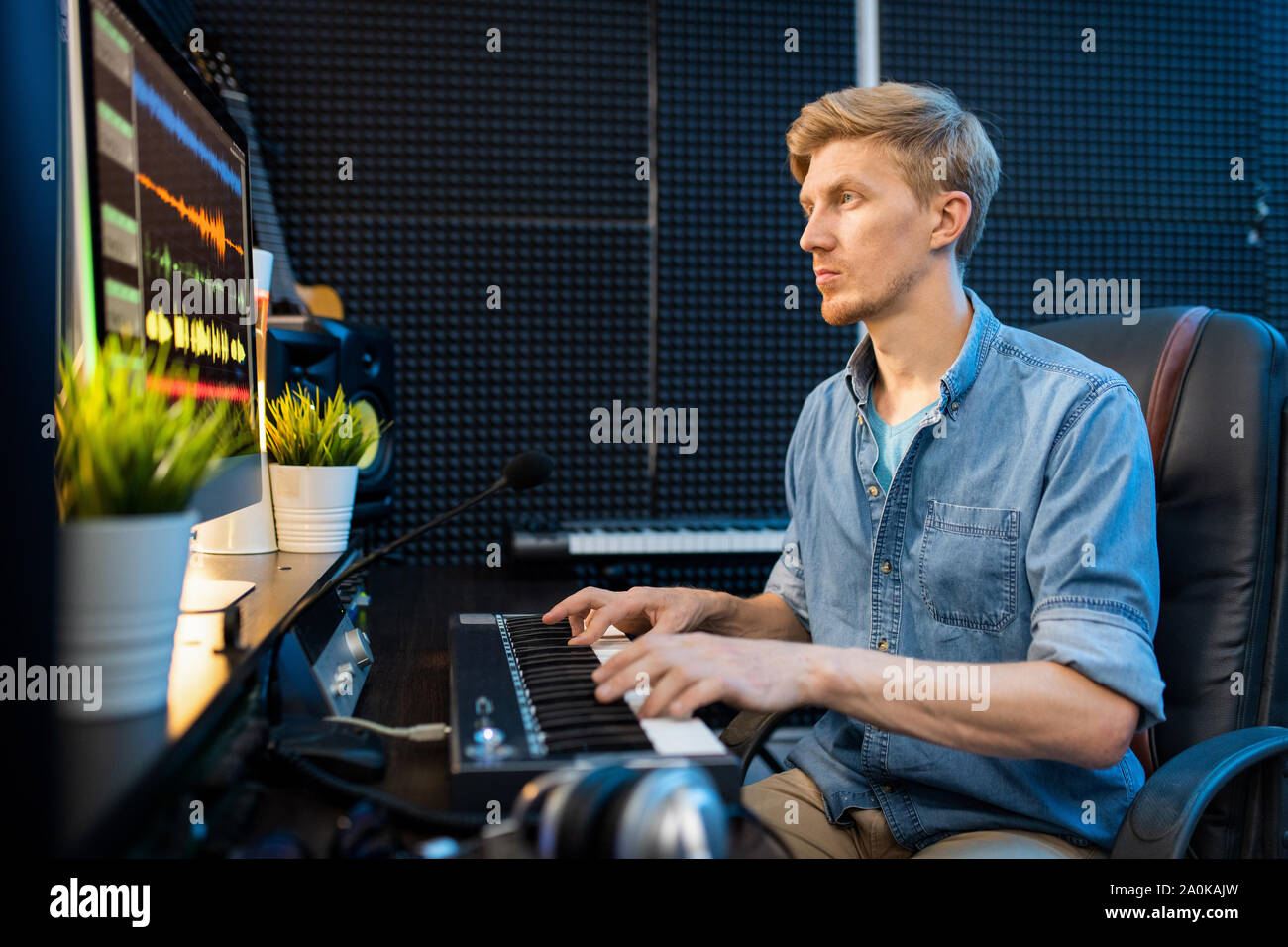 Young man looking at computer screen while pressing keys of piano ...