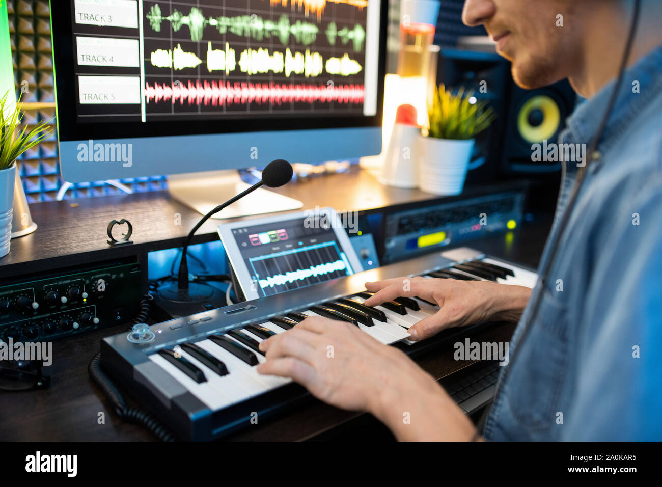 Young musician sitting by workplace and pressing keys of piano keyboard ...