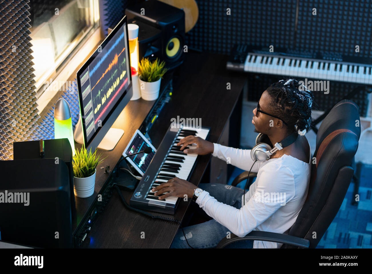 Young musician of African ethnicity sitting by workplace in studio of ...