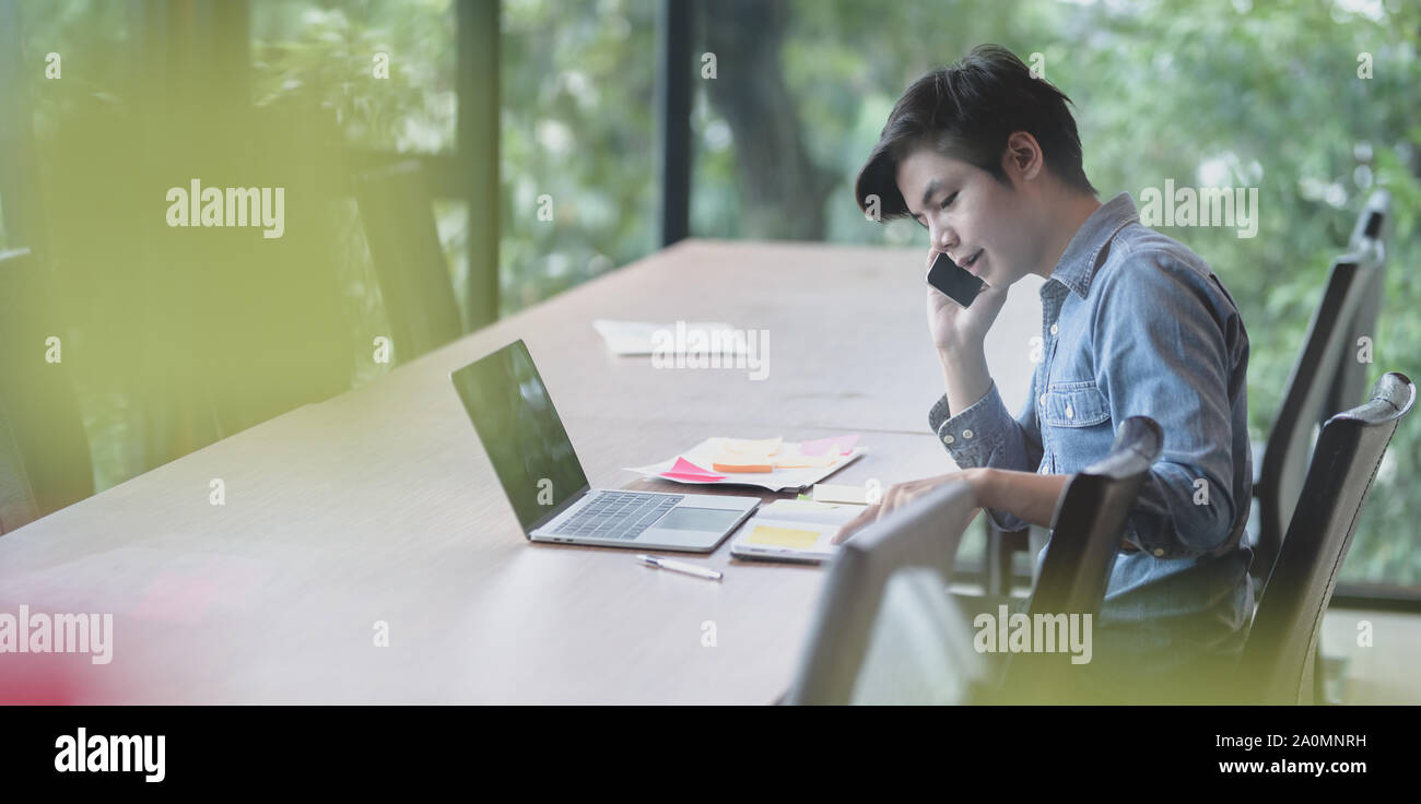 Young UX web developer working on laptop computer while having a phone ...