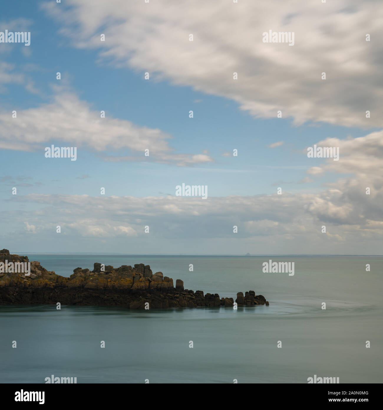 Square format view of a rocky cliff outcrop in a calm ocean under an ...