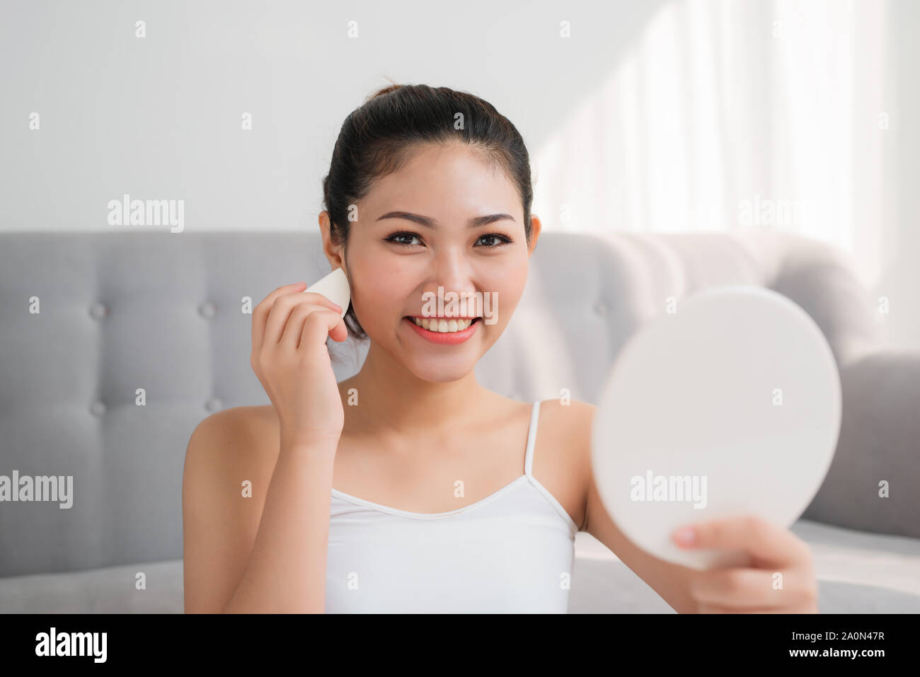 Beautiful asian woman using cosmetic sponge on face and look mirror at ...