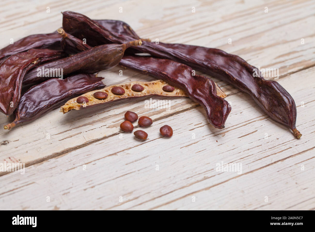 Carob. Organic carob pods with seeds and leaves on white wooden table ...