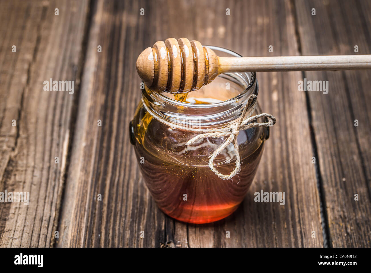 Glass pot of honey and wooden stick with dripping honey on rustic ...