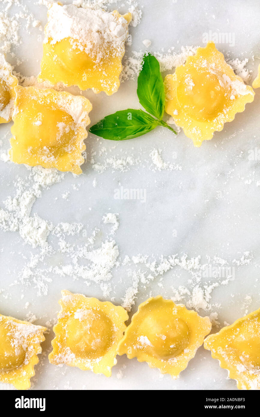 Ravioli with flour and basil leaves, forming a frame, shot from the top ...