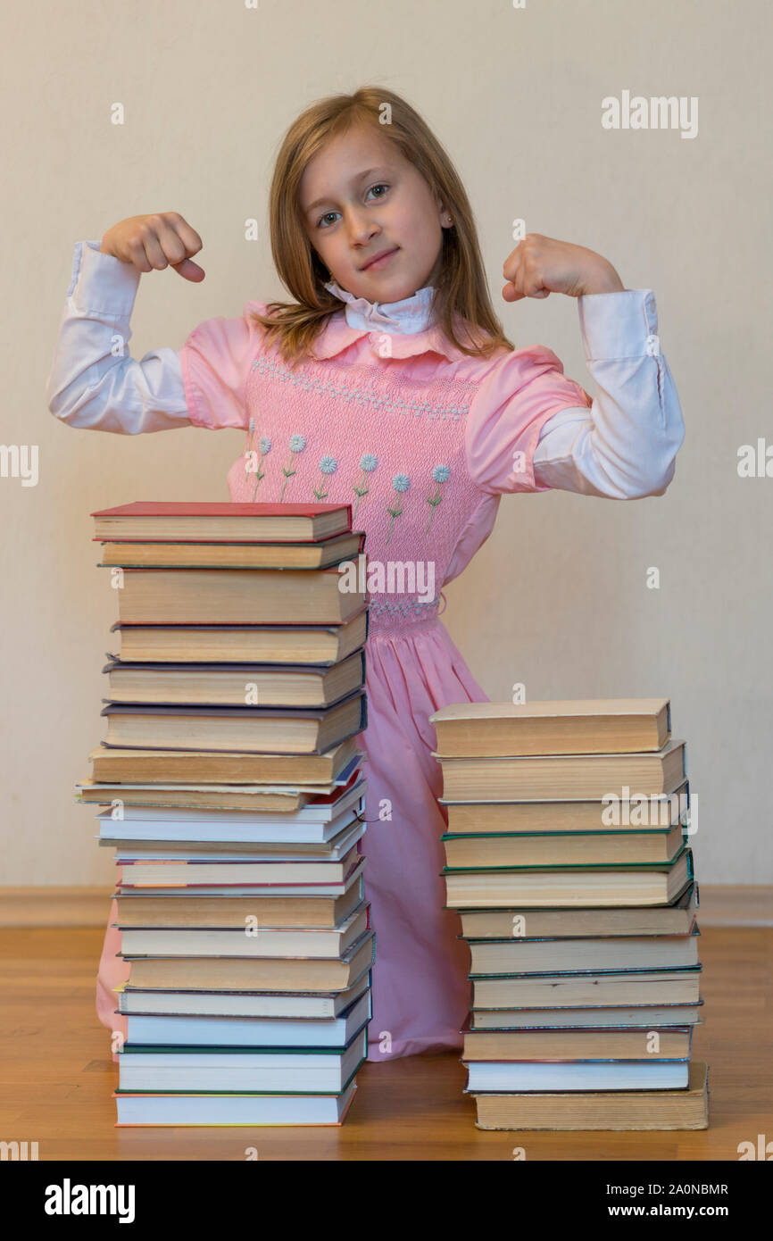 Concept The power of knowledge. A girl with a pile of books shows her ...