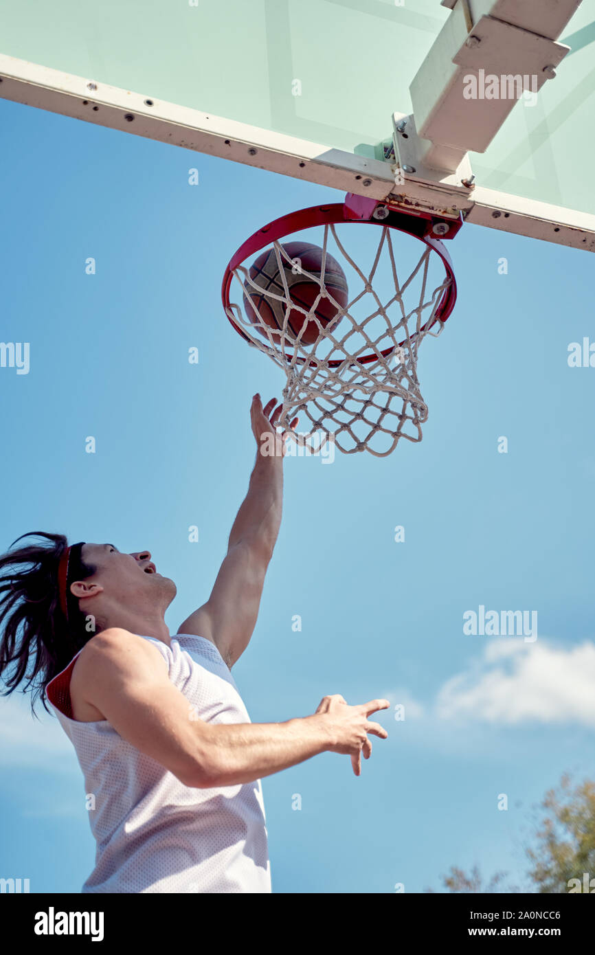 Image of athlete man throwing ball into basketball hoop on sports field ...